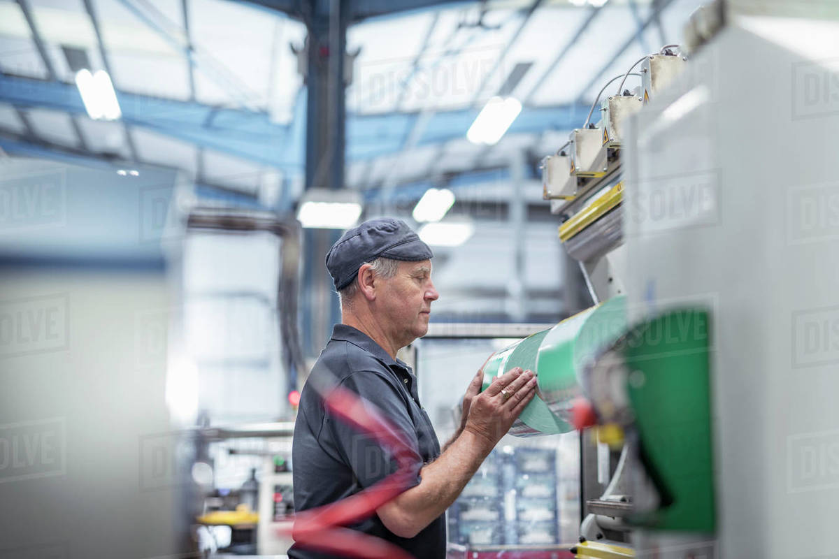 Worker loading plastic packaging in print machine in print factory ...