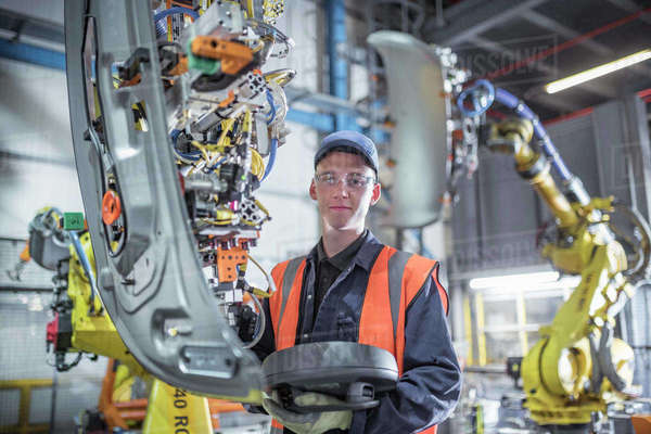 Portrait of apprentice engineer programming robots in car factory ...
