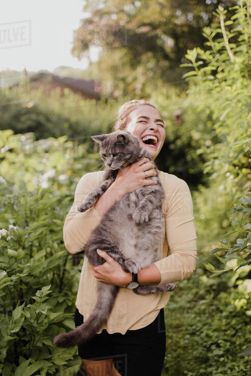 Woman gardener carrying cat in garden - Stock Photo - Dissolve