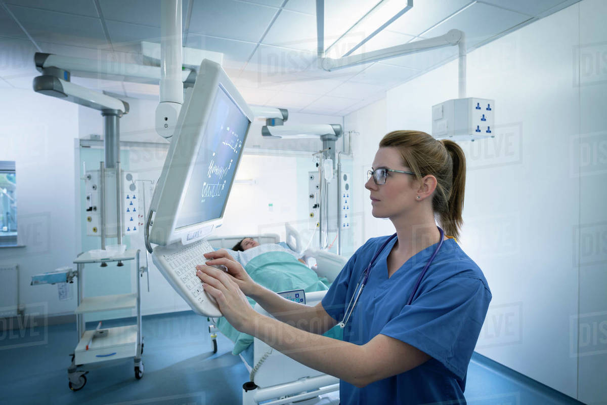 Nurse inspecting screen in intensive care unit in hospital setting ...