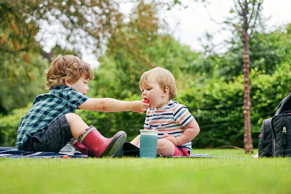 Brothers sharing food in park - Royalty-free Stock Photo | Dissolve