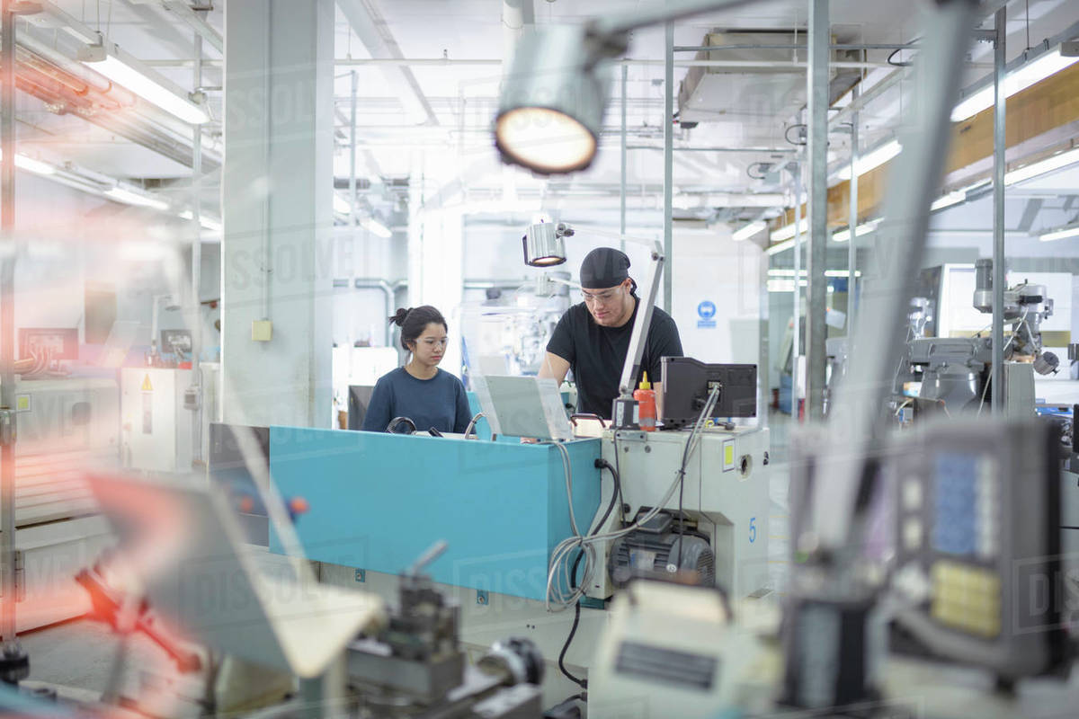 Female and male engineers working at lathes in engineering factory ...