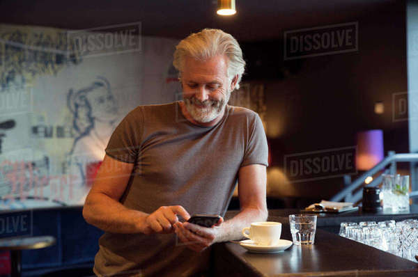 A man leaning on a bar beside a coffee cup, smiling and looking at a ...