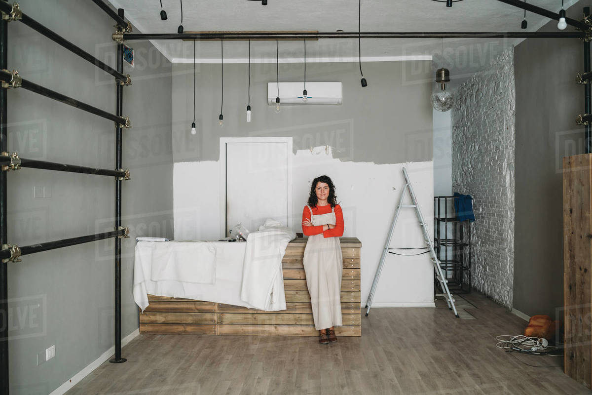 Mid adult woman leaning against table in her new shop, full length ...