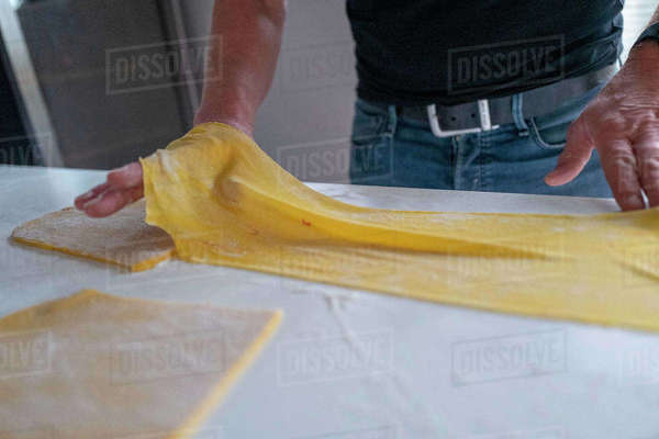 Hands skillfully stretching fresh pasta dough on a kitchen counter ...