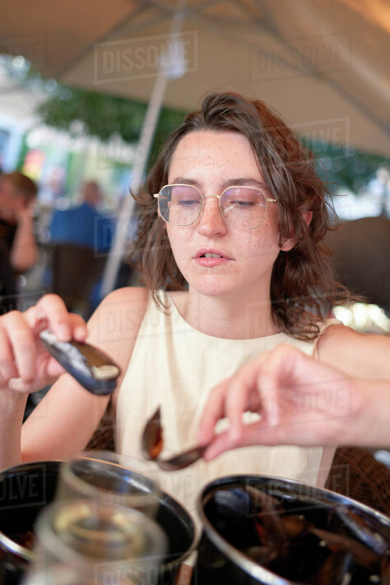 A woman sitting on a stone ledge by a marina at dusk, wearing a yellow ...