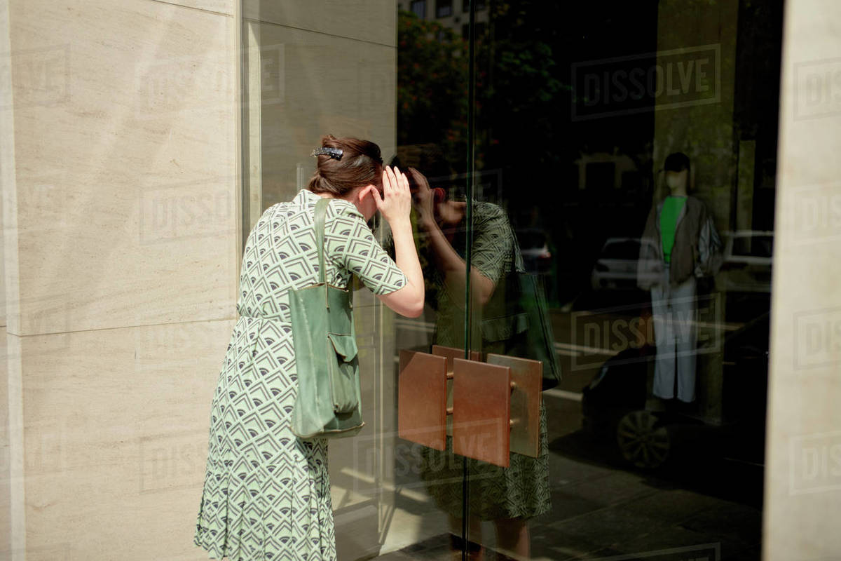 Woman in a patterned dress looking at a storefront window, her ...