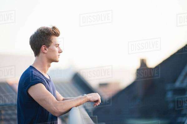 Young man on rooftop, looking at view - Stock Photo - Dissolve