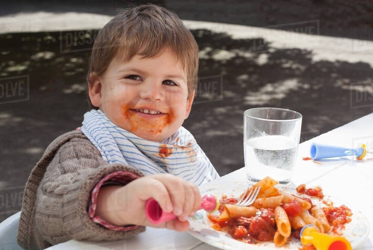 Toddler boy eating pasta outdoors - Royalty-free Stock Photo | Dissolve
