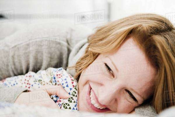 Smiling woman laying on bed - Stock Photo - Dissolve