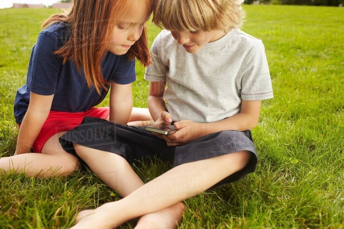 Children using cell phone in grass - Stock Photo - Dissolve