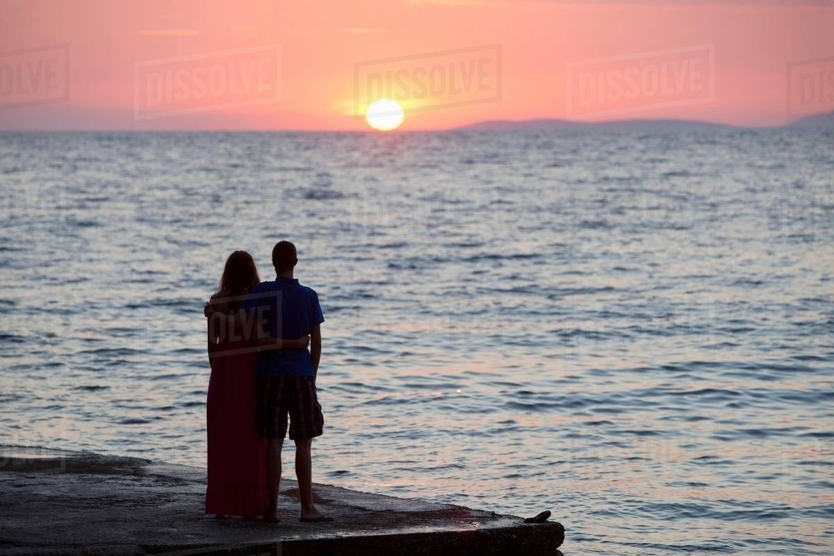 Couple watching sunset on pier - Royalty-free Stock Photo | Dissolve