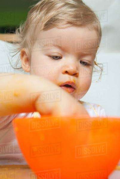 Baby girl with hand in orange bowl - Stock Photo - Dissolve