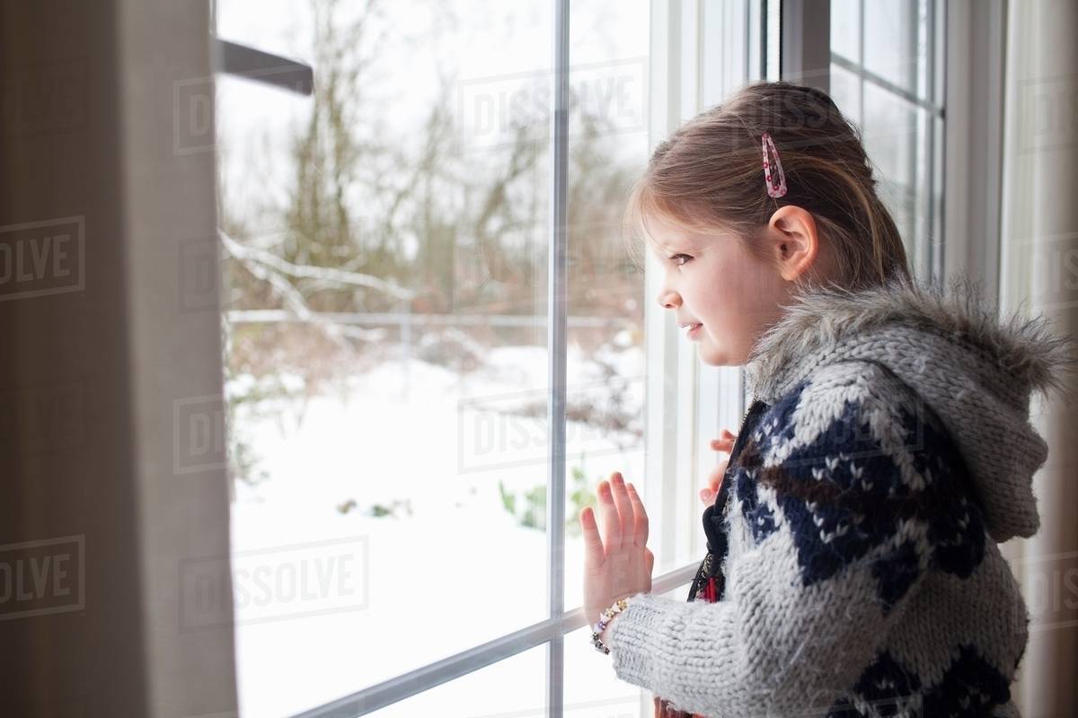 Young girl looking out of window at garden in snow - Stock Photo - Dissolve