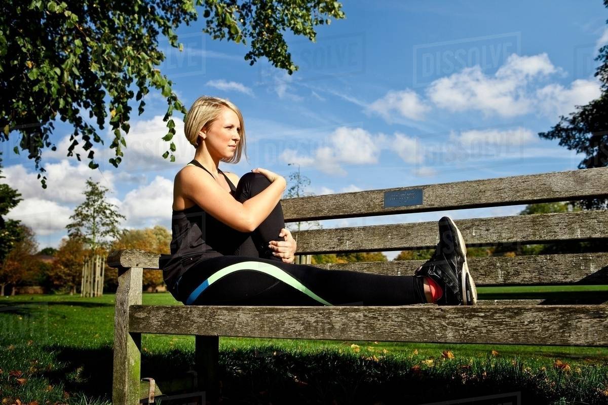 Woman bending leg on park bench - Royalty-free Stock Photo | Dissolve