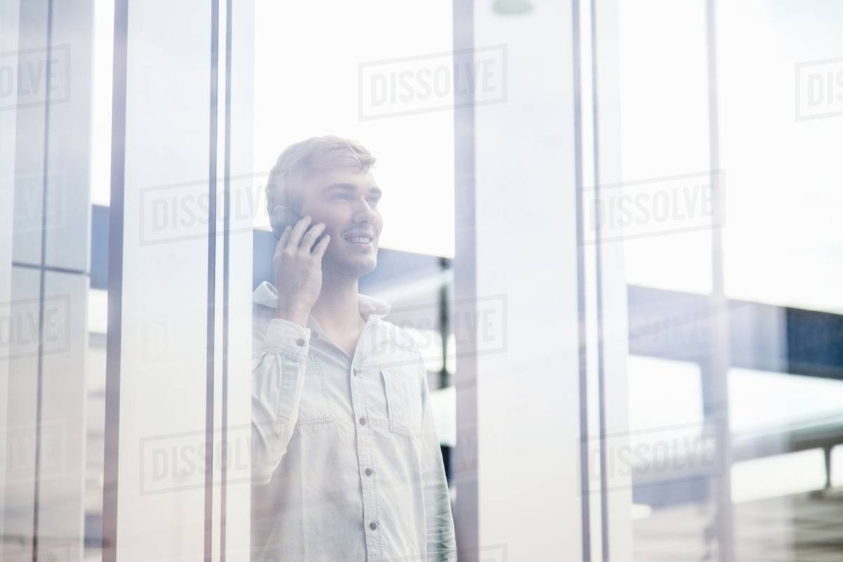 Young man behind reflective glass talking on smartphone - Royalty-free ...