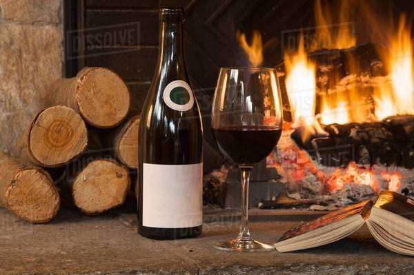 Glass of wine and book by fireplace - Royalty-free Stock Photo | Dissolve