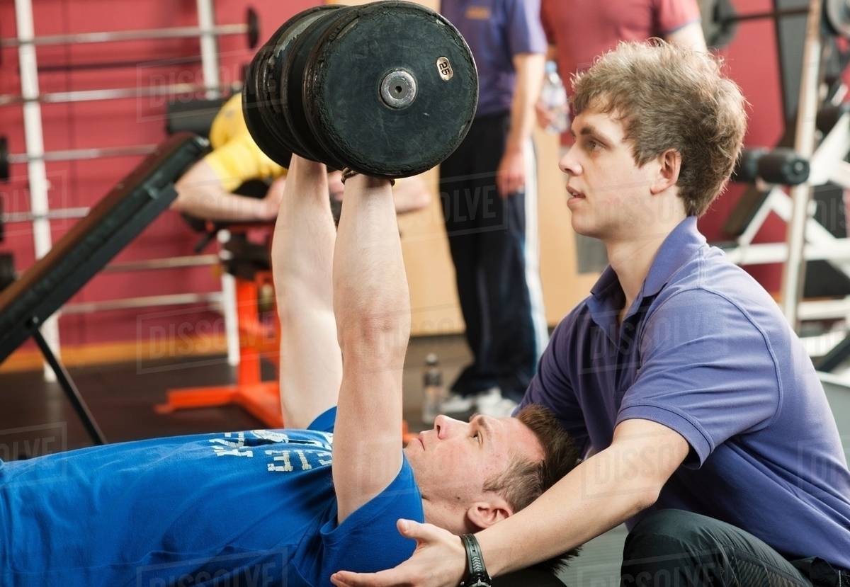 Trainer helping man lift weights at gym - Royalty-free Stock Photo ...
