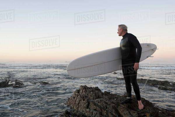 Surfer standing on rocky beach - Stock Photo - Dissolve