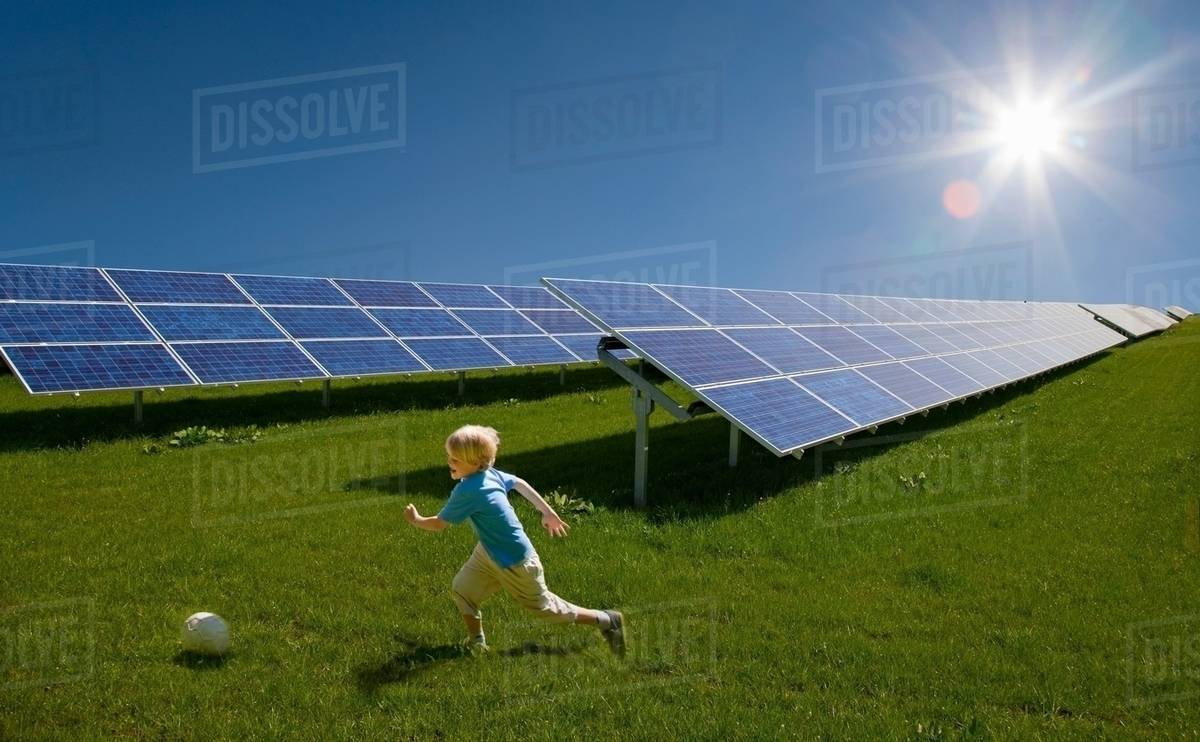 Boy playing in field by solar panels - Stock Photo - Dissolve