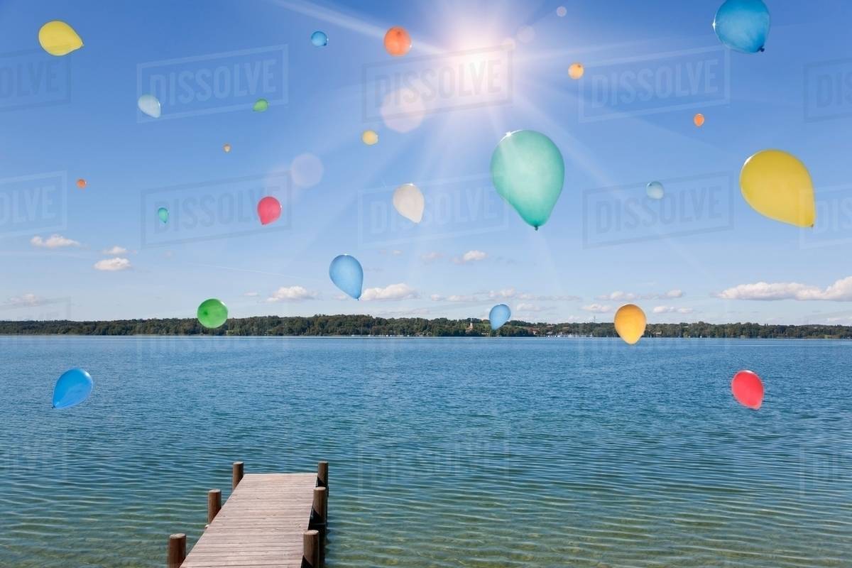 Balloons floating over still lake - Stock Photo - Dissolve
