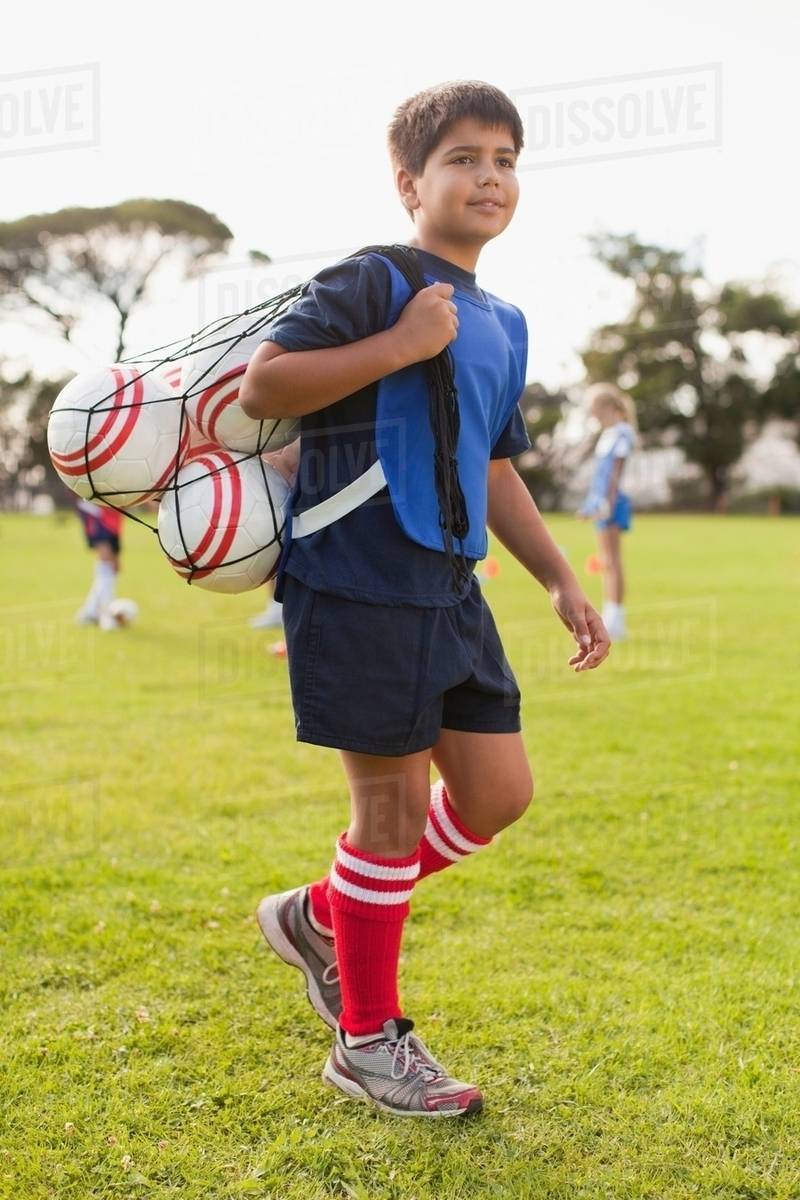 Boy carrying soccer balls on pitch - Royalty-free Stock Photo | Dissolve
