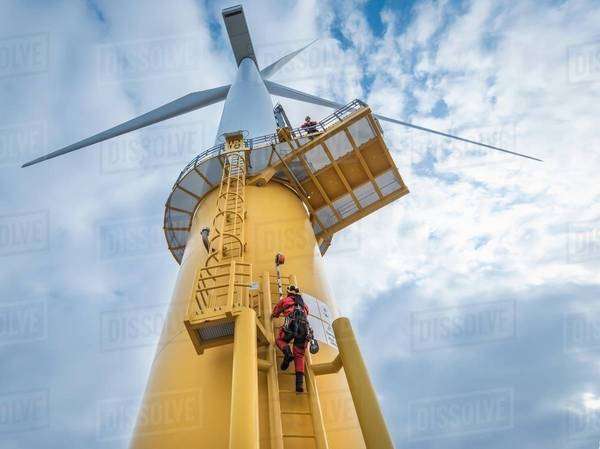 Engineers climbing wind turbine from boat at offshore windfarm, low ...
