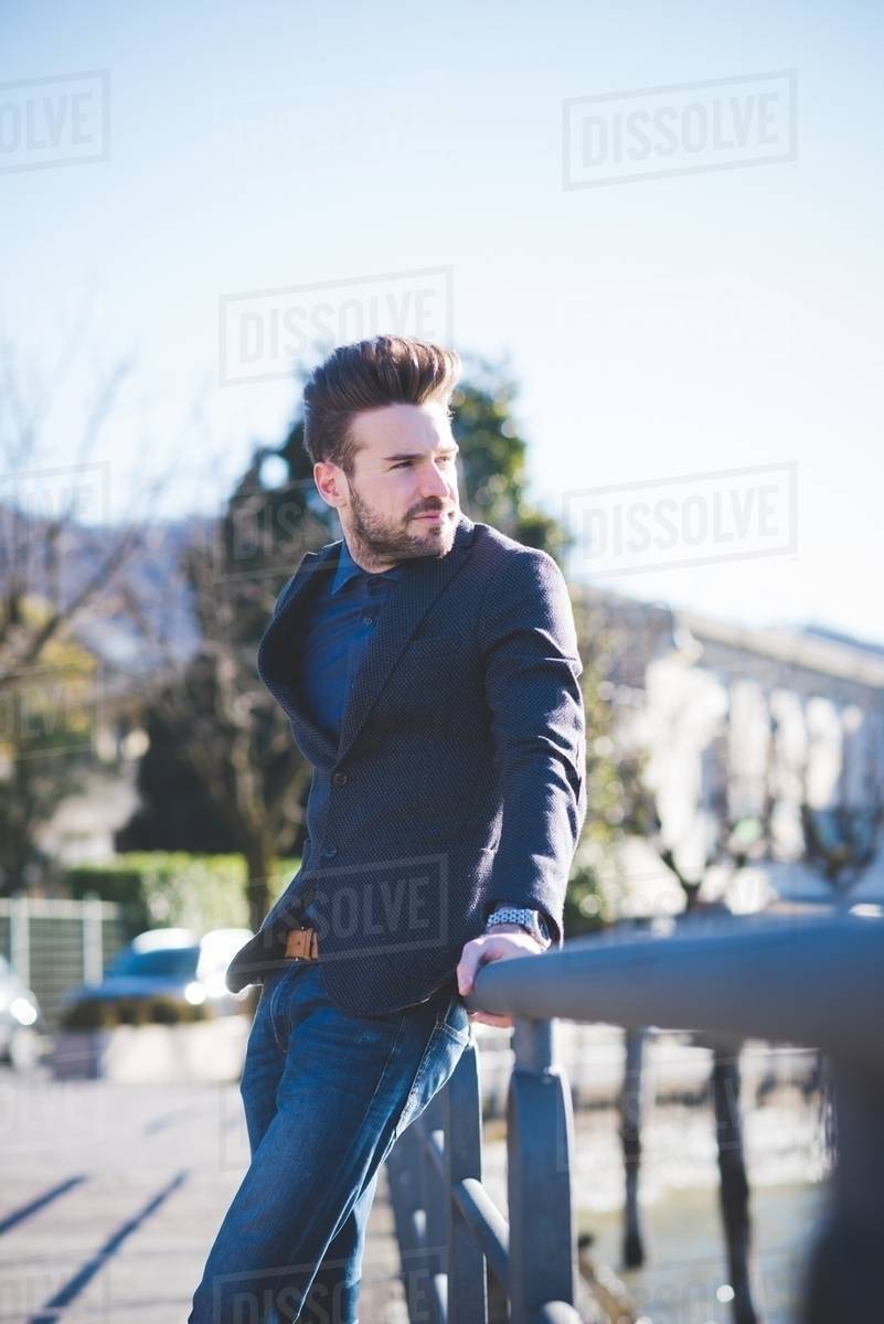 Young man leaning against railing and looking over his shoulder ...