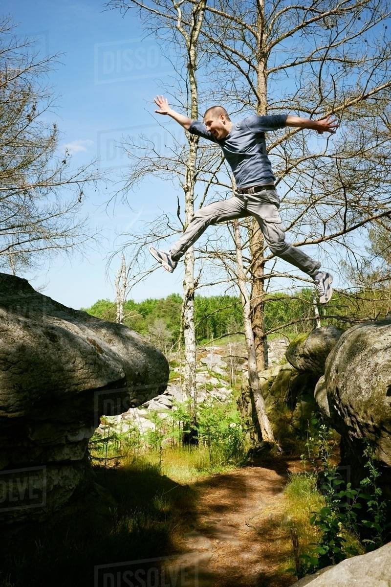Mid adult man jumping across forest boulders - Royalty-free Stock Photo ...
