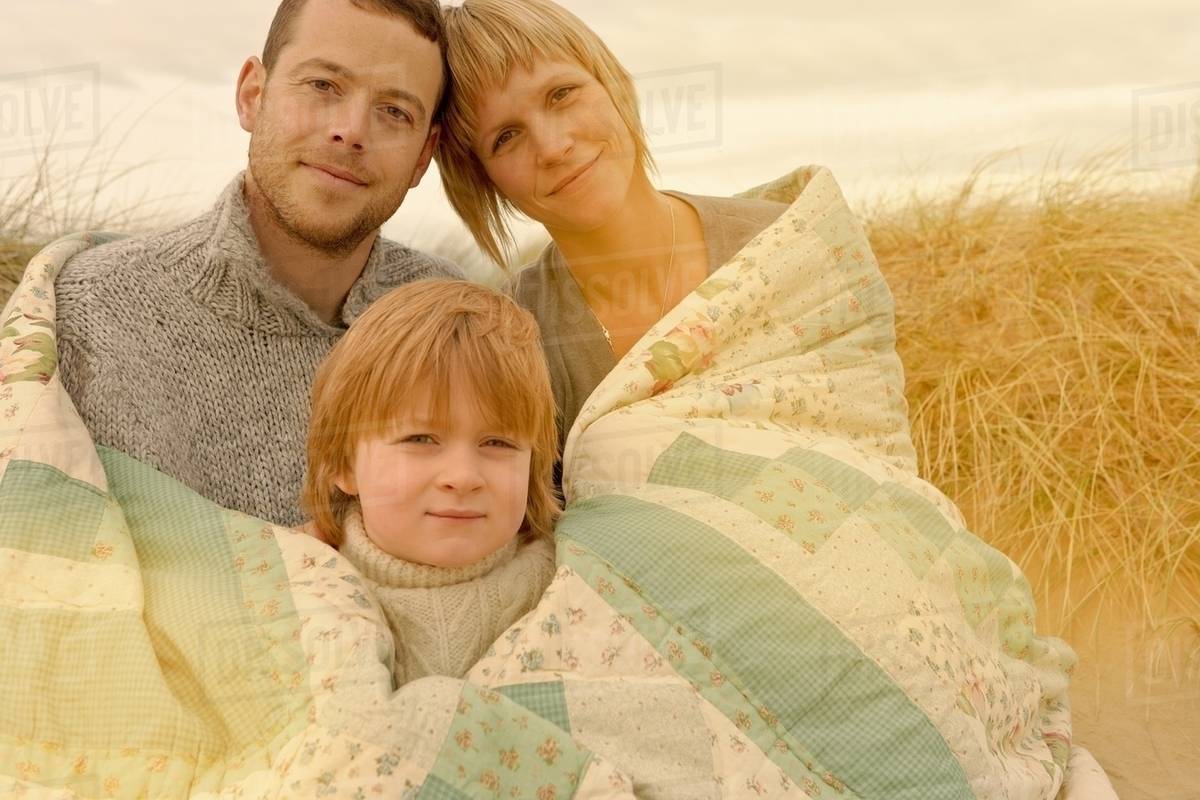 Family cuddling under quilt on beach - Royalty-free Stock Photo | Dissolve