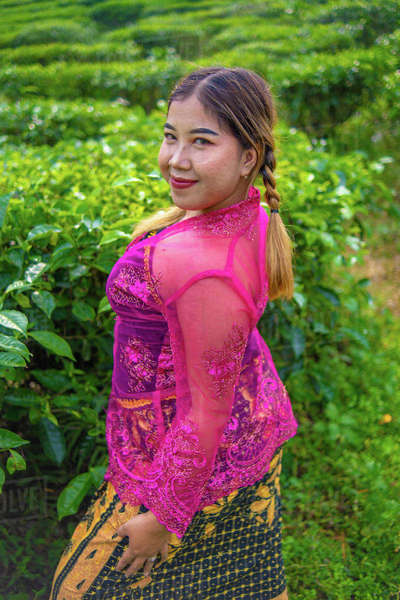 an Asian woman in a pink costume is posing in front of a tea plantation ...
