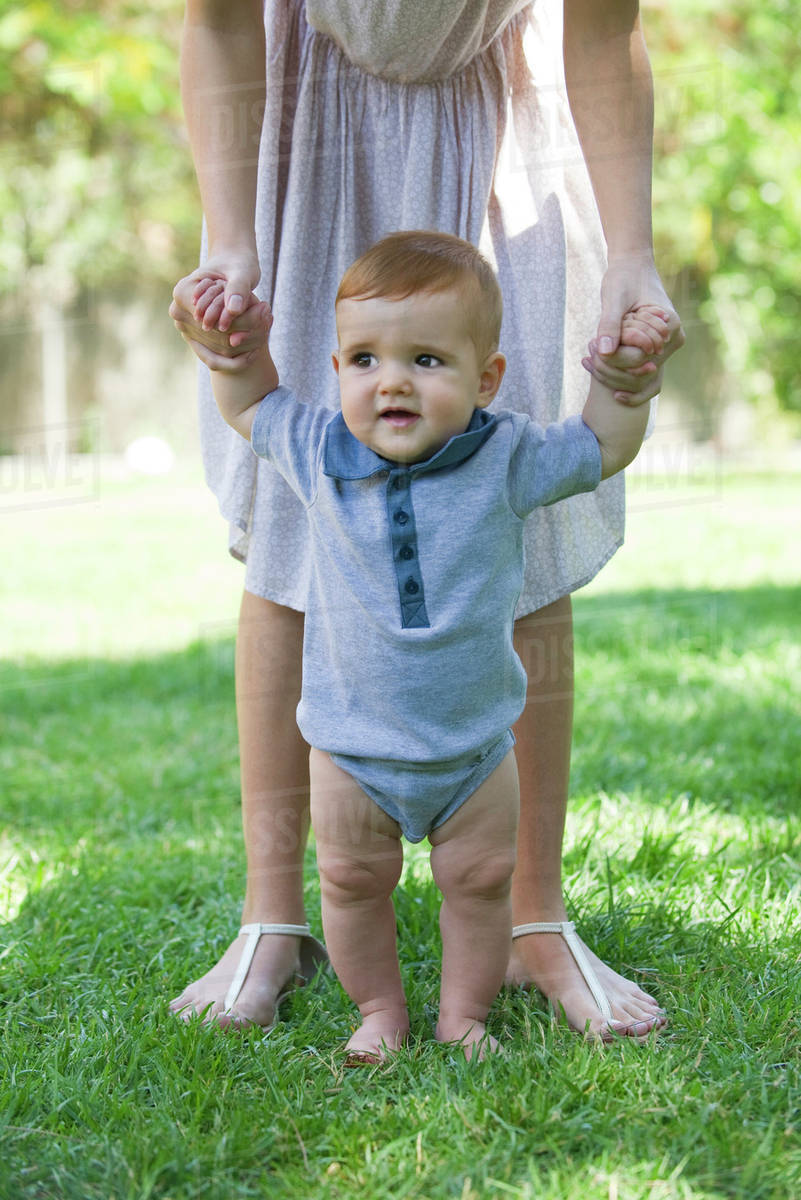 Baby standing outdoors, holding mother's hands for support - Stock ...