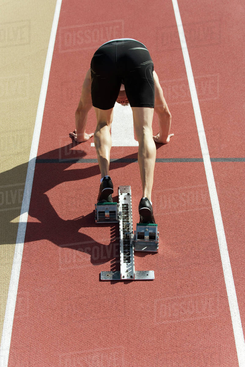 Runner crouched at startling line, rear view - Stock Photo - Dissolve