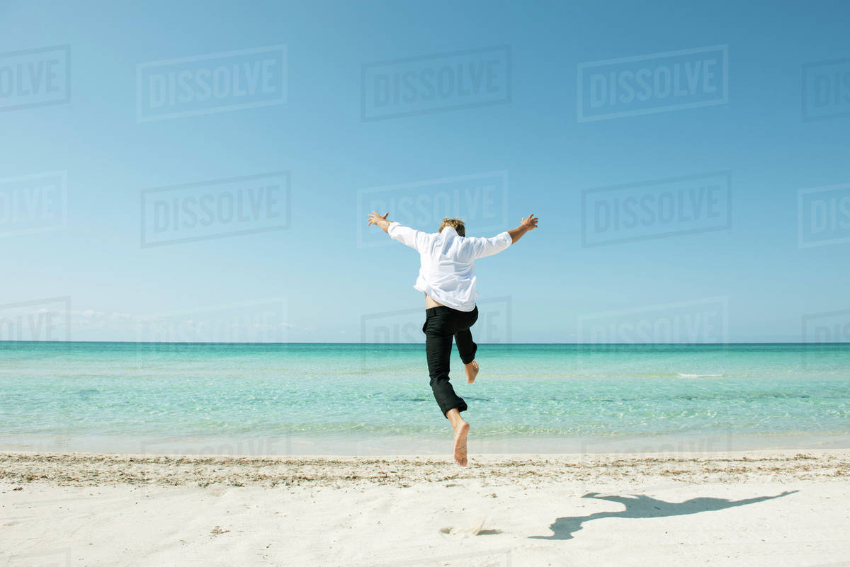 Man jumping midair on beach, rear view - Royalty-free Stock Photo ...