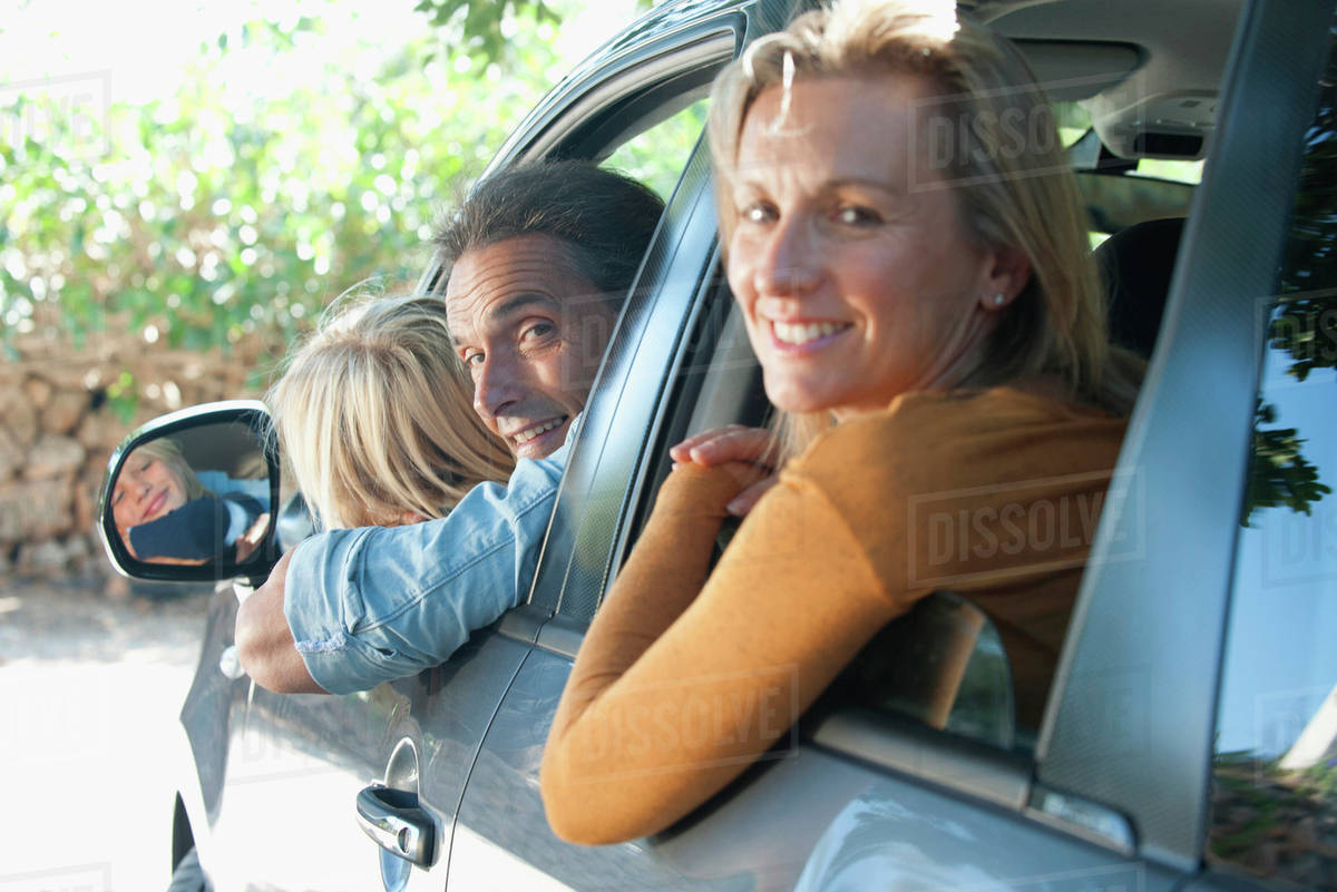 Family together in car, leaning out windows and smiling over shoulders ...