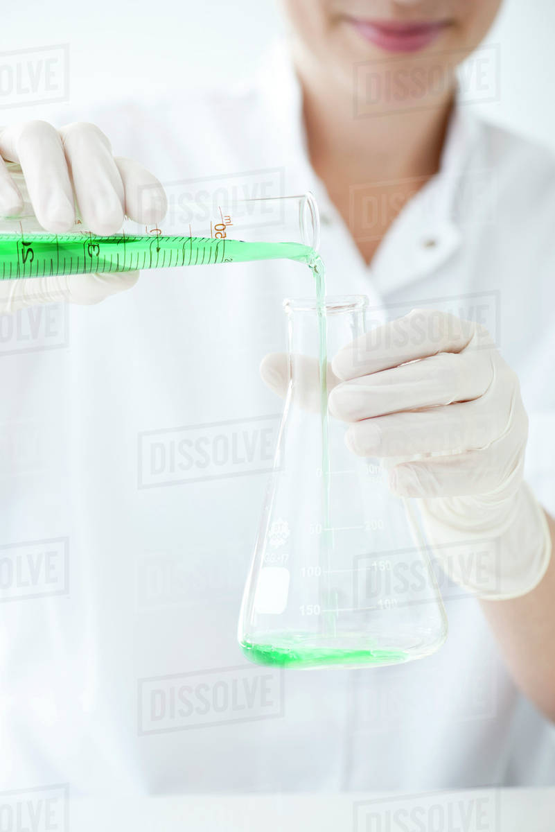 Scientist pouring liquid from graduated cylinder to conical flask ...