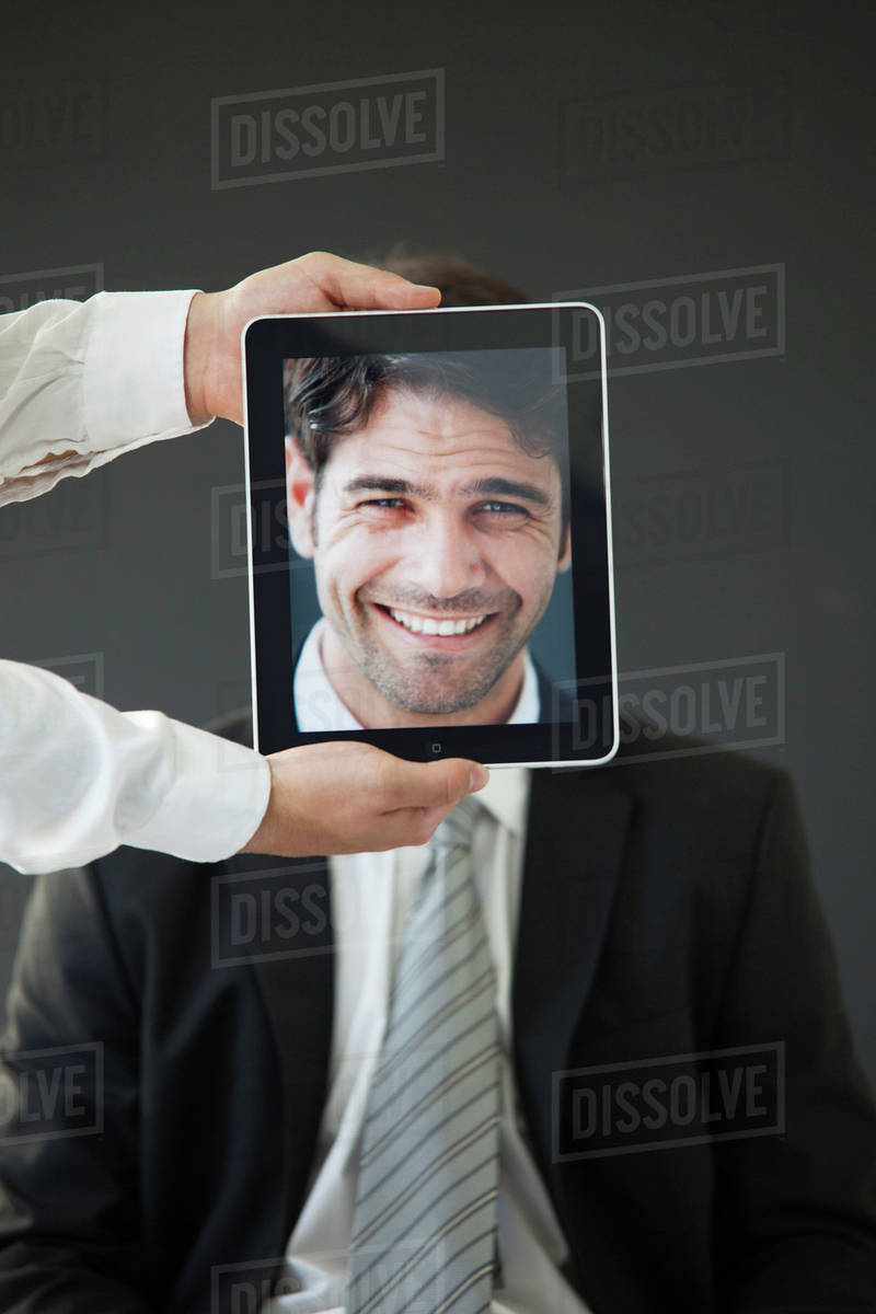 Man concealed behind digital tablet displaying image of smiling man ...