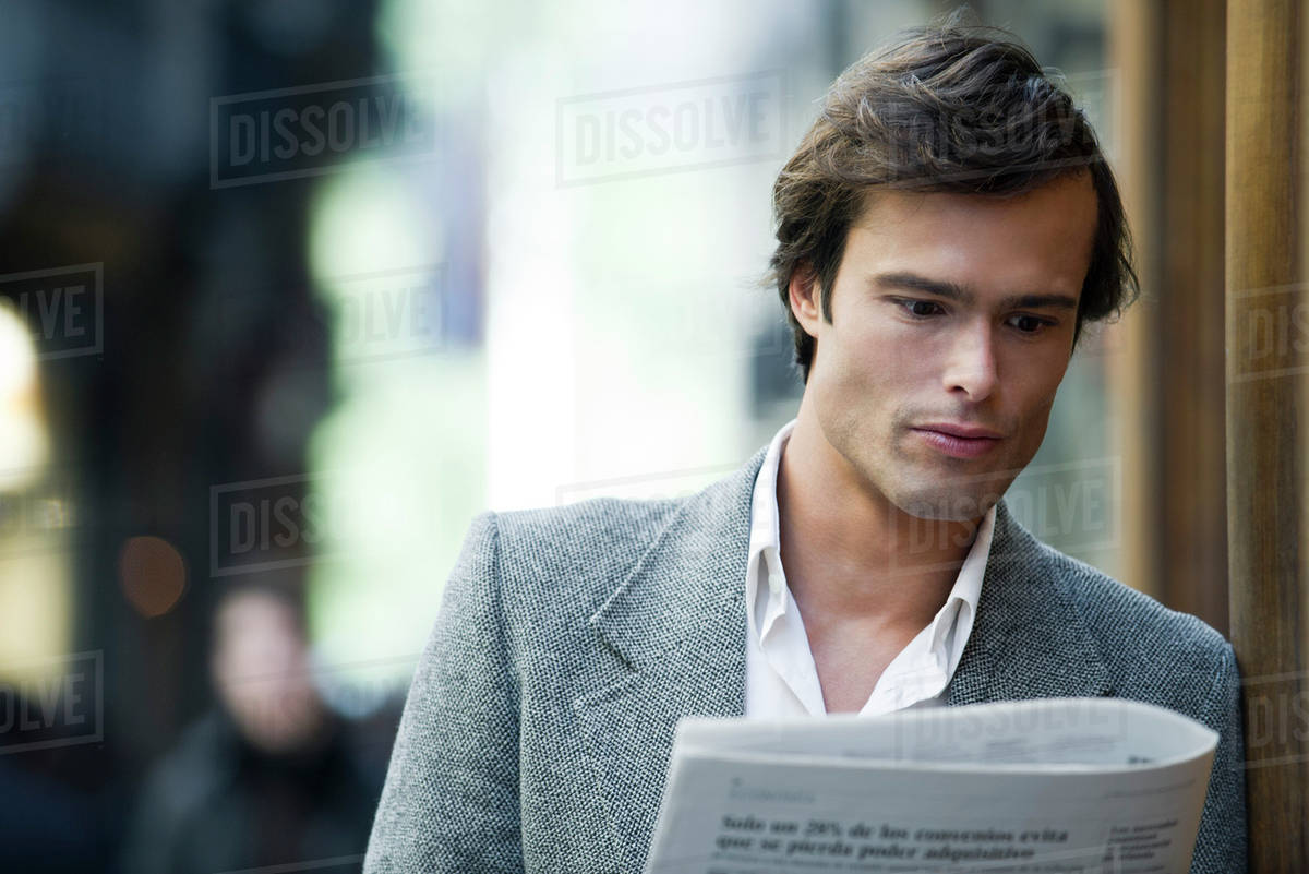 Man leaning against wall reading newspaper - Stock Photo - Dissolve