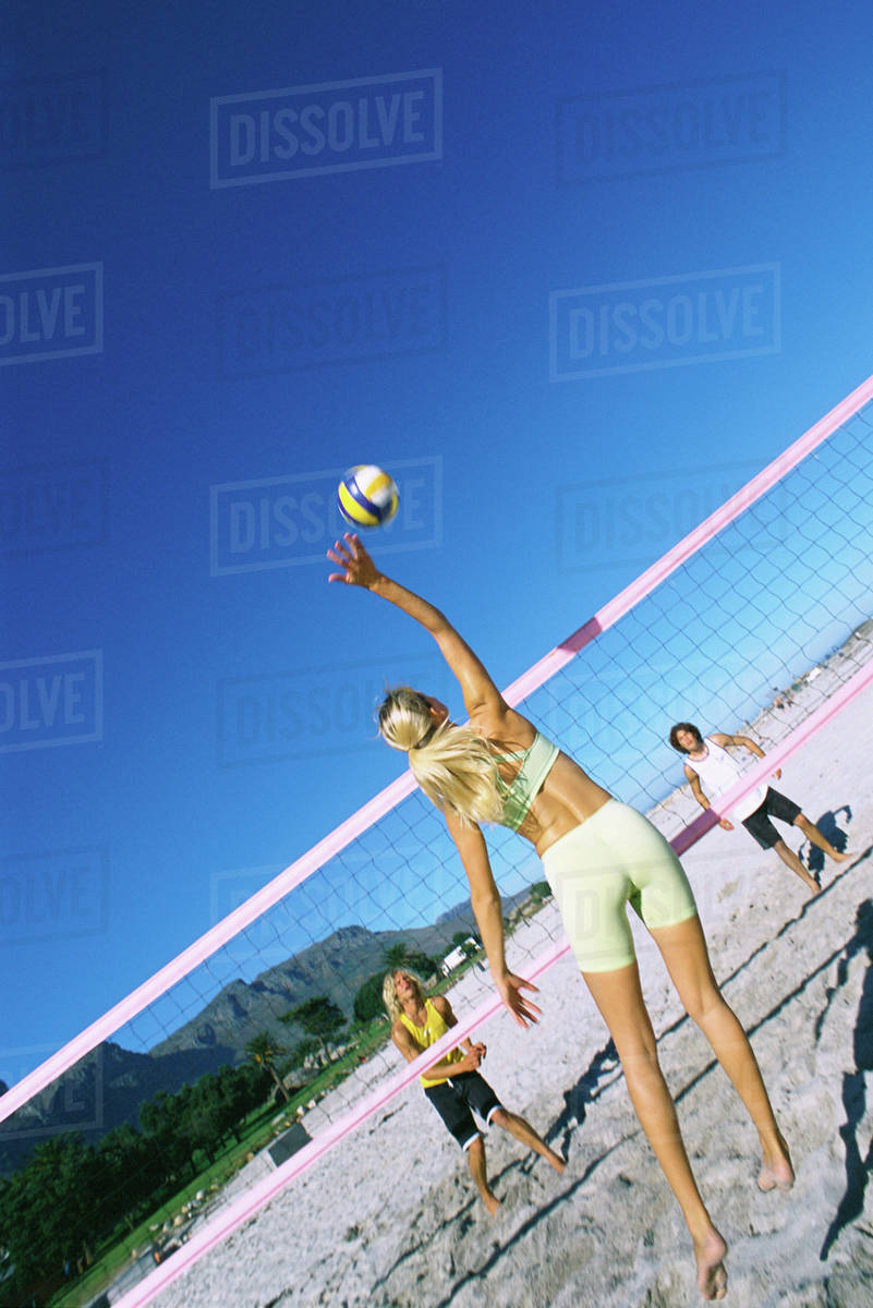 Female jumping to hit volleyball over net - Stock Photo - Dissolve