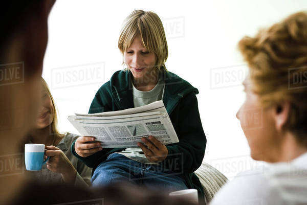 Boy reading newspaper, family members in foreground - Royalty-free ...