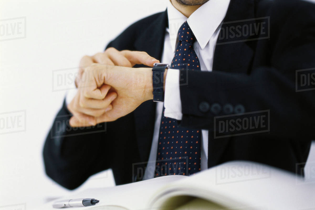Businessman checking time on wristwatch, cropped - Stock Photo - Dissolve