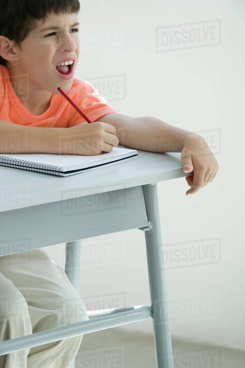 Elementary school student taking notes in classroom, squinting at board ...