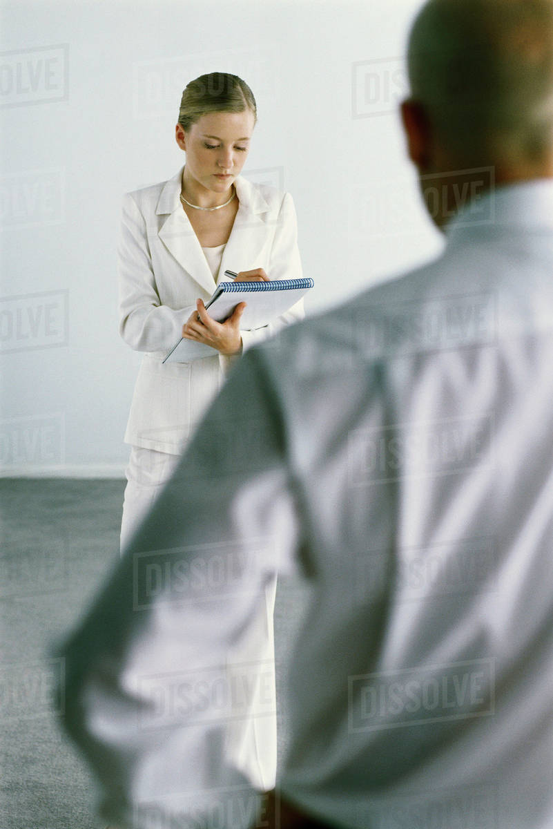 Young assistant standing taking notes, boss dictating in foreground ...