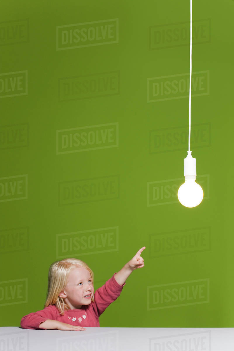 Little girl pointing at illuminated light bulb suspended overhead ...