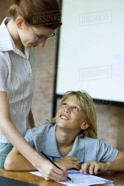 Student looking up at teacher smiling as they grade their classwork ...