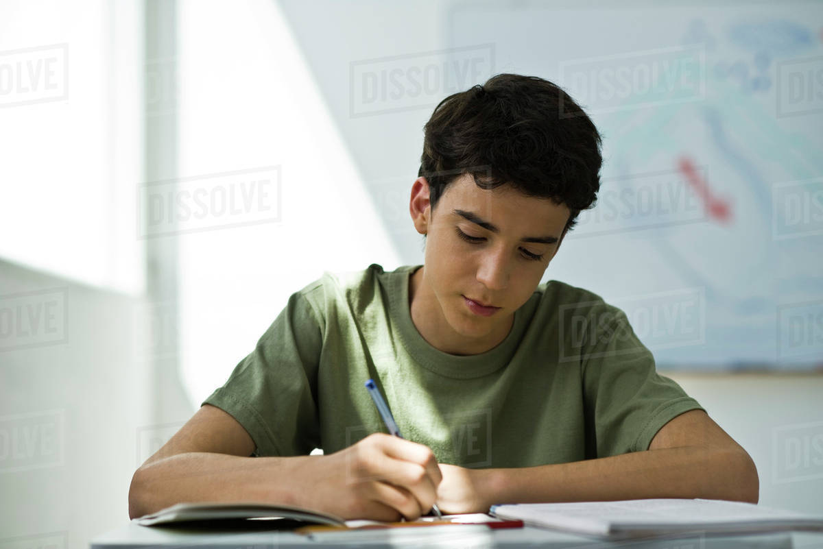 Teenage boy focusing on classwork assignment - Stock Photo - Dissolve
