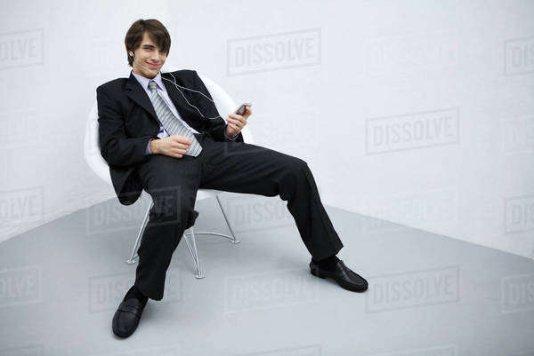 Young man in suit leaning back in chair, listening to mp3 player ...