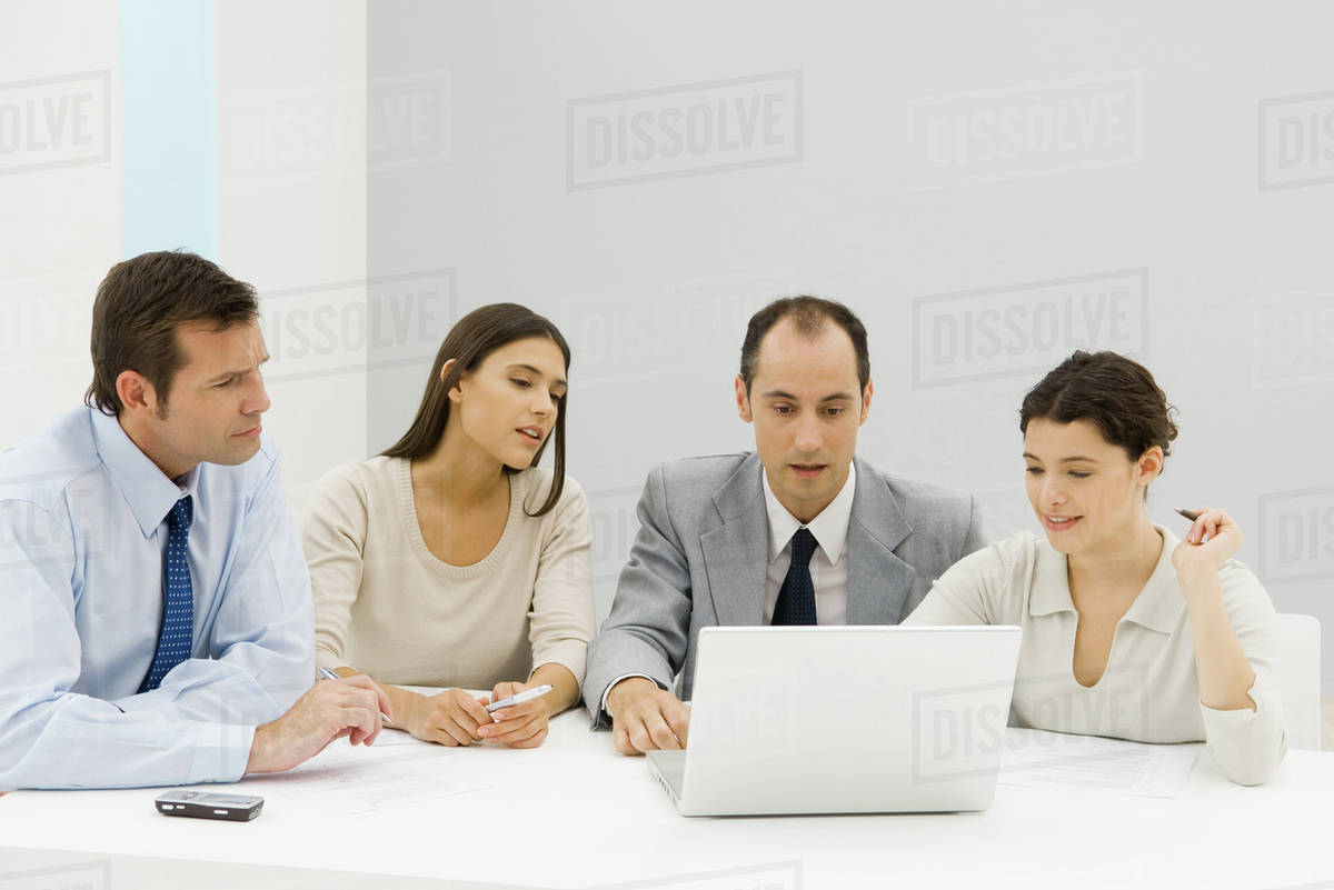 Team of business associates looking at laptop computer together in ...