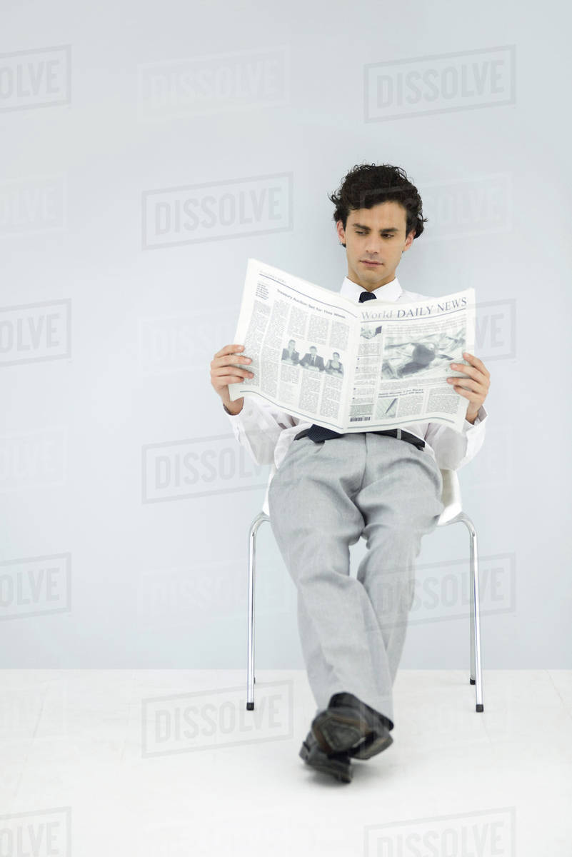 Businessman slouching in chair, reading newspaper - Stock Photo - Dissolve
