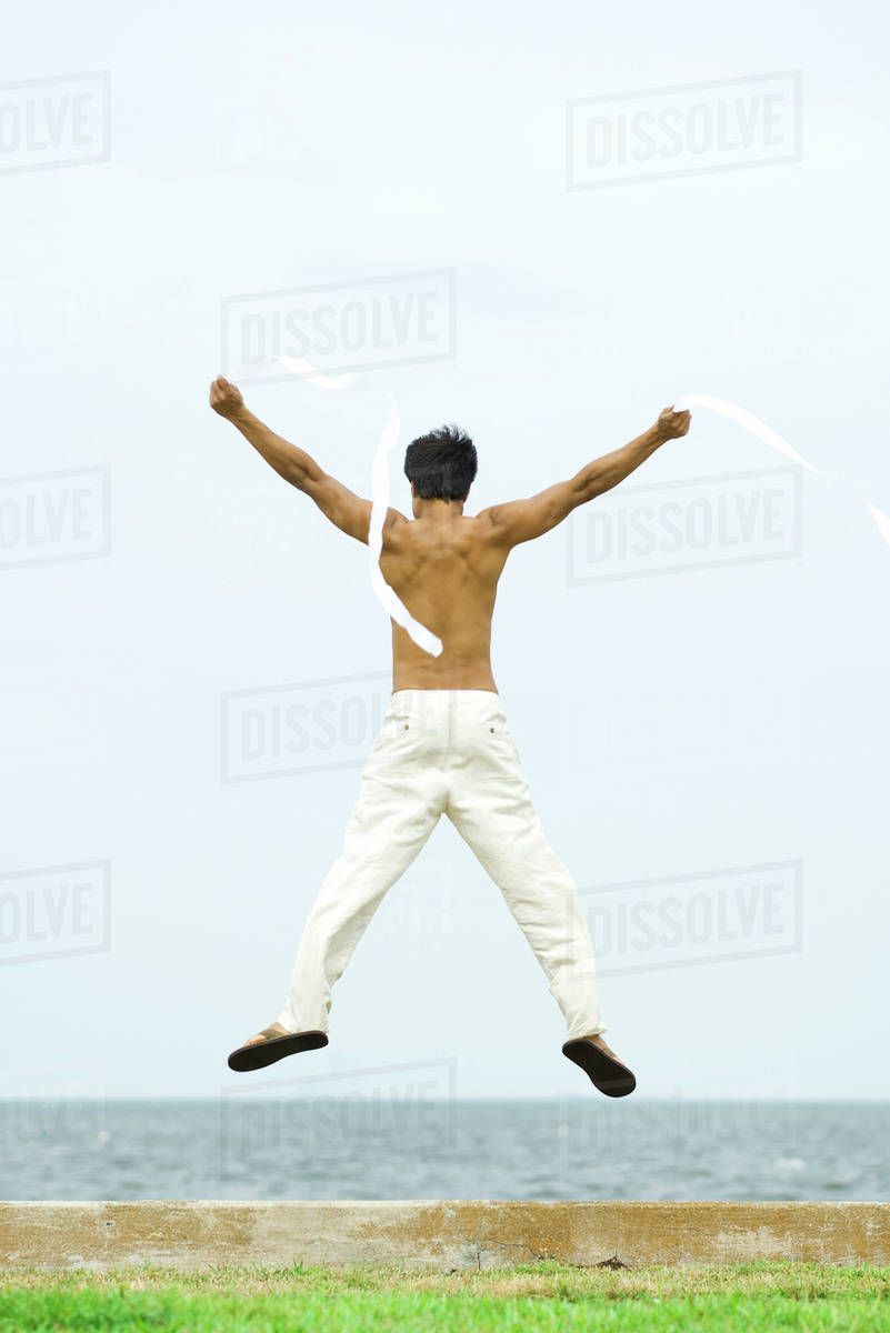 Man jumping into the air with streamers in hands, rear view, ocean ...